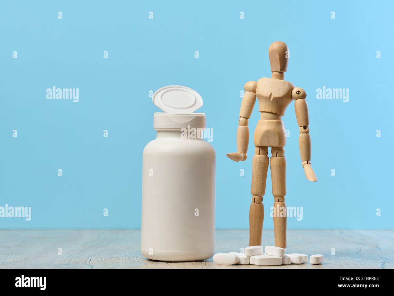 Wooden dummy and plastic bottle and oval white pills on the table, blue ...