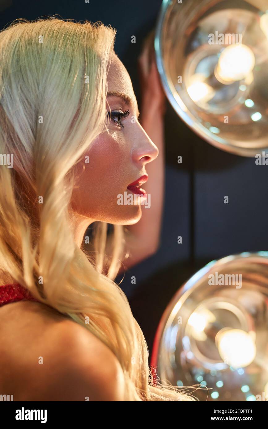 Profile of beautiful blonde lady with long wavy hair lit by light bulbs ...