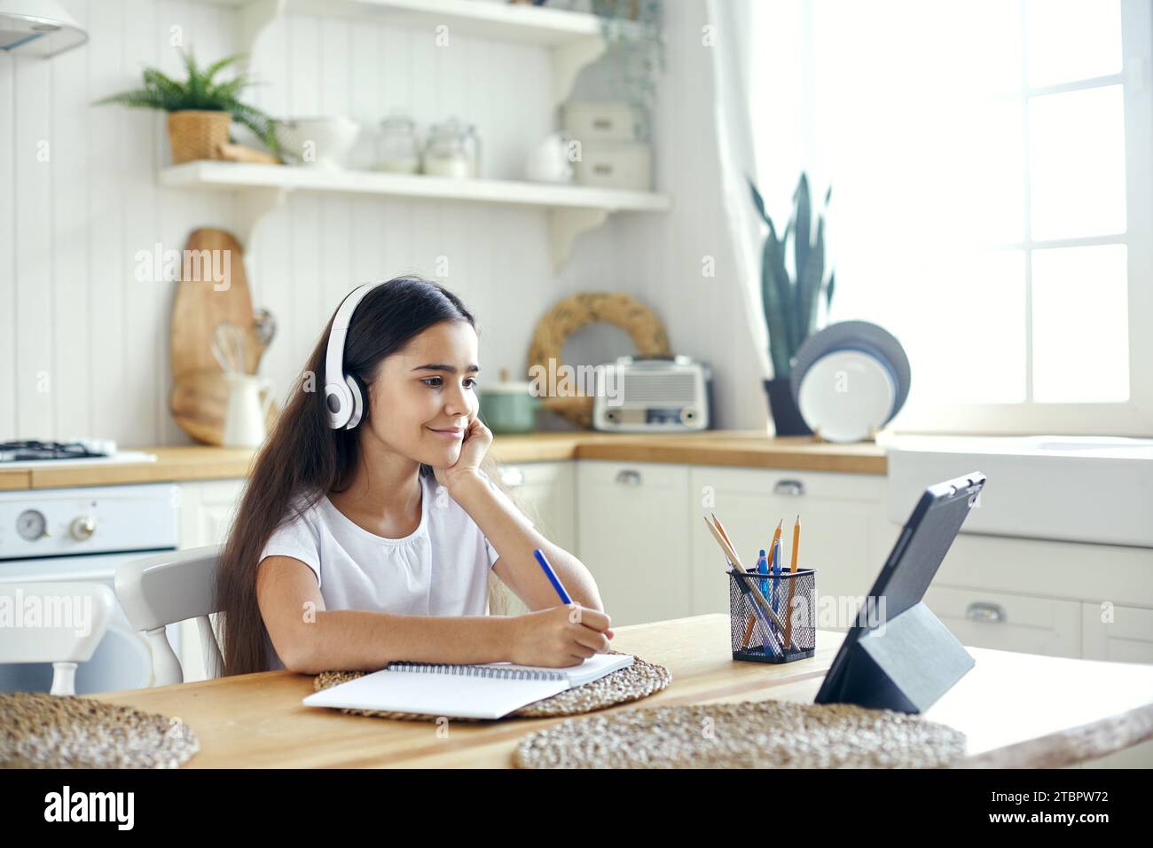 Pretty pre-teen 12s girl in wireless headphones sit at table e-learning ...