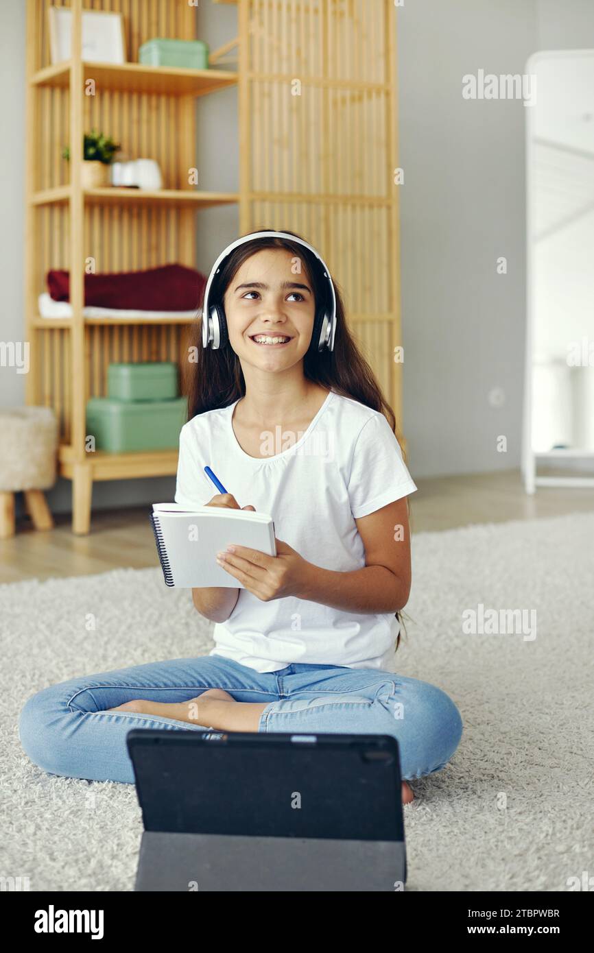 Pretty pre-teen girl sit on floor in cozy living room wear wireless ...