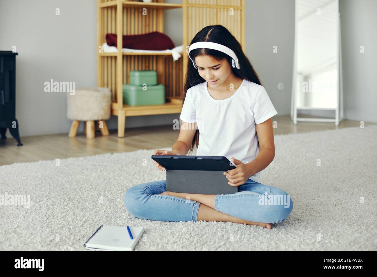 Pretty pre-teen girl sit on floor in cozy living room wear wireless ...