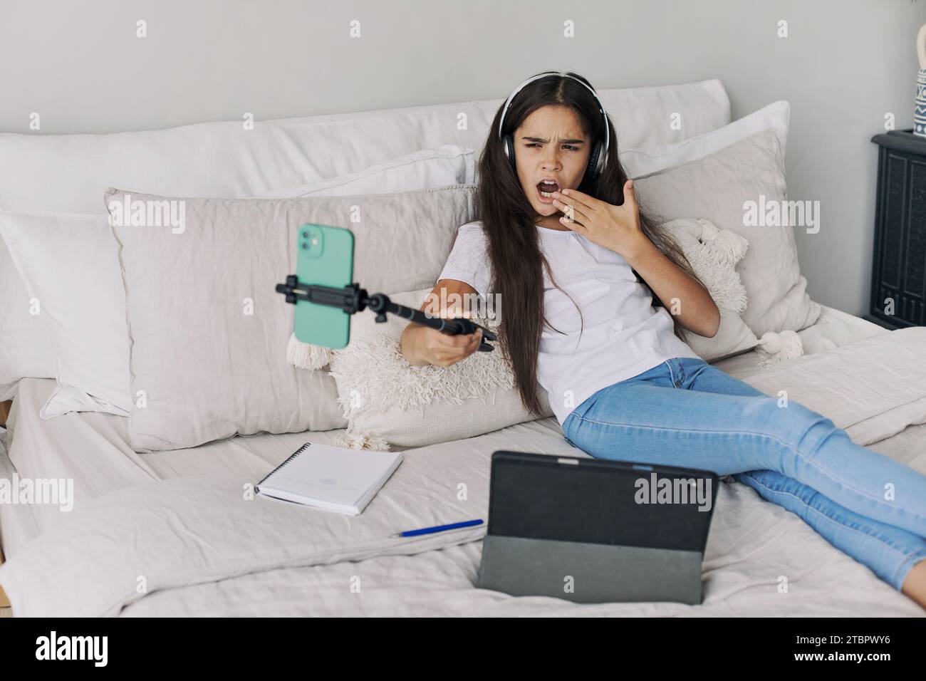 Attractive pre-teen girl resting seated on bed in bedroom holding ...