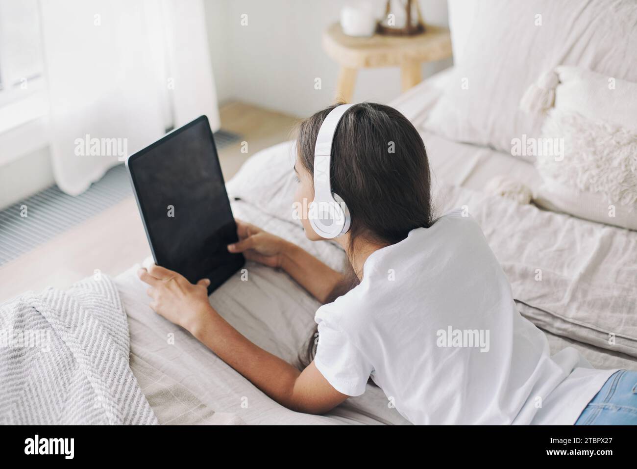 Adorable 12s pre-teen girl in wireless headphones lying on bed with ...