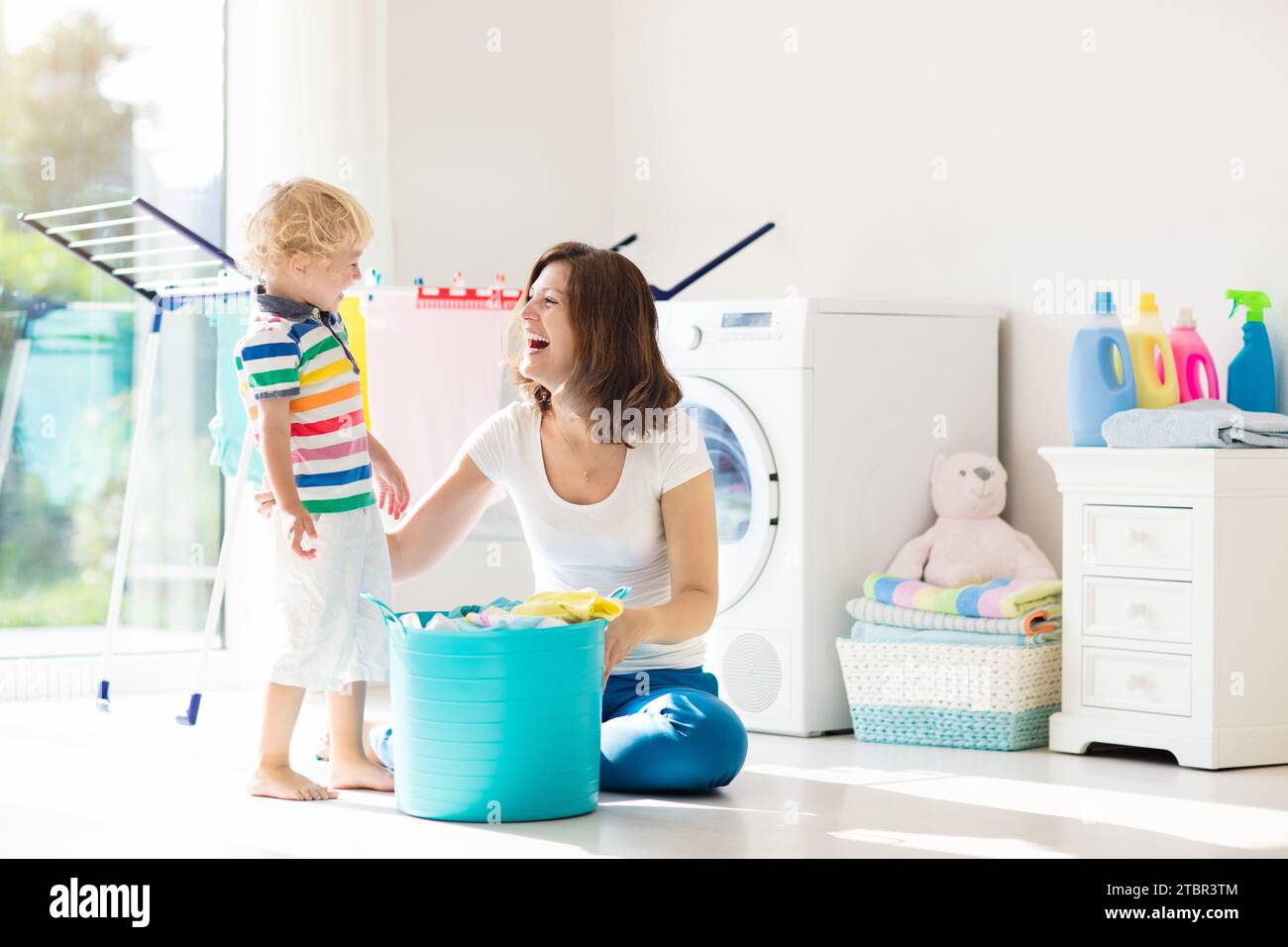 Mother and kids in laundry room with washing machine or tumble dryer ...