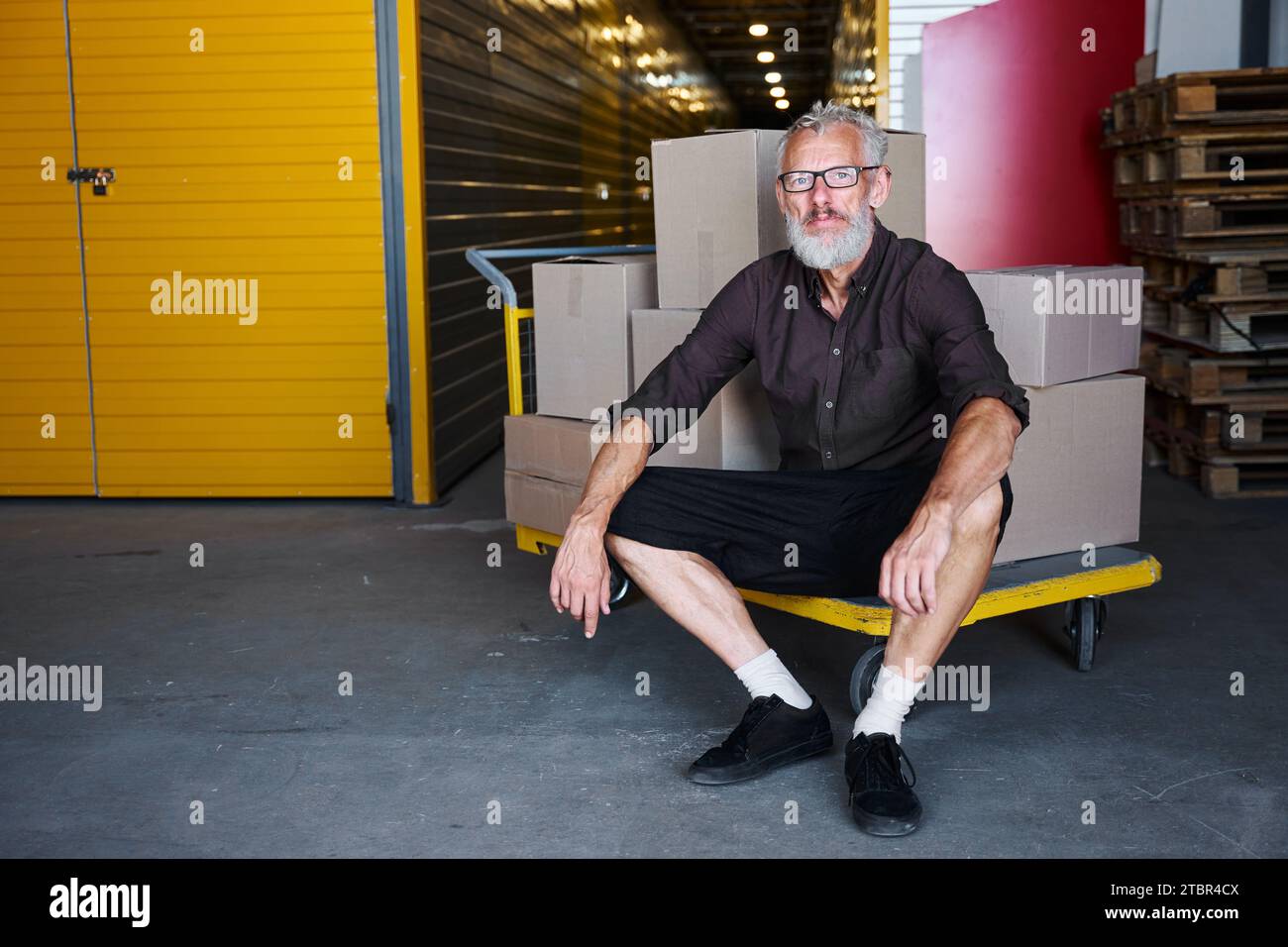 Man with glasses sat down to rest on cart with boxes Stock Photo - Alamy