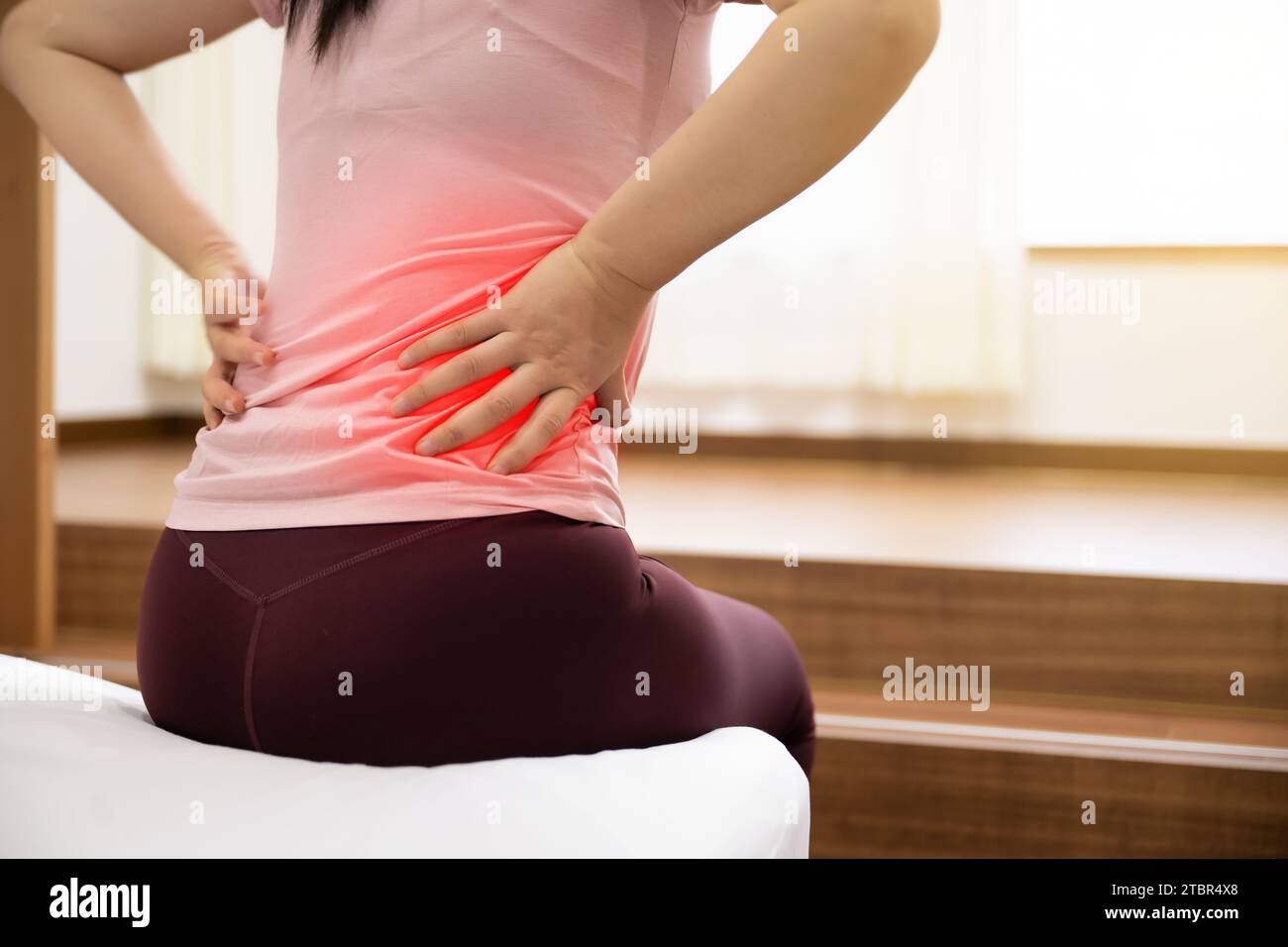 A woman sitting on a bed and holding her sore waist with her hand (the ...