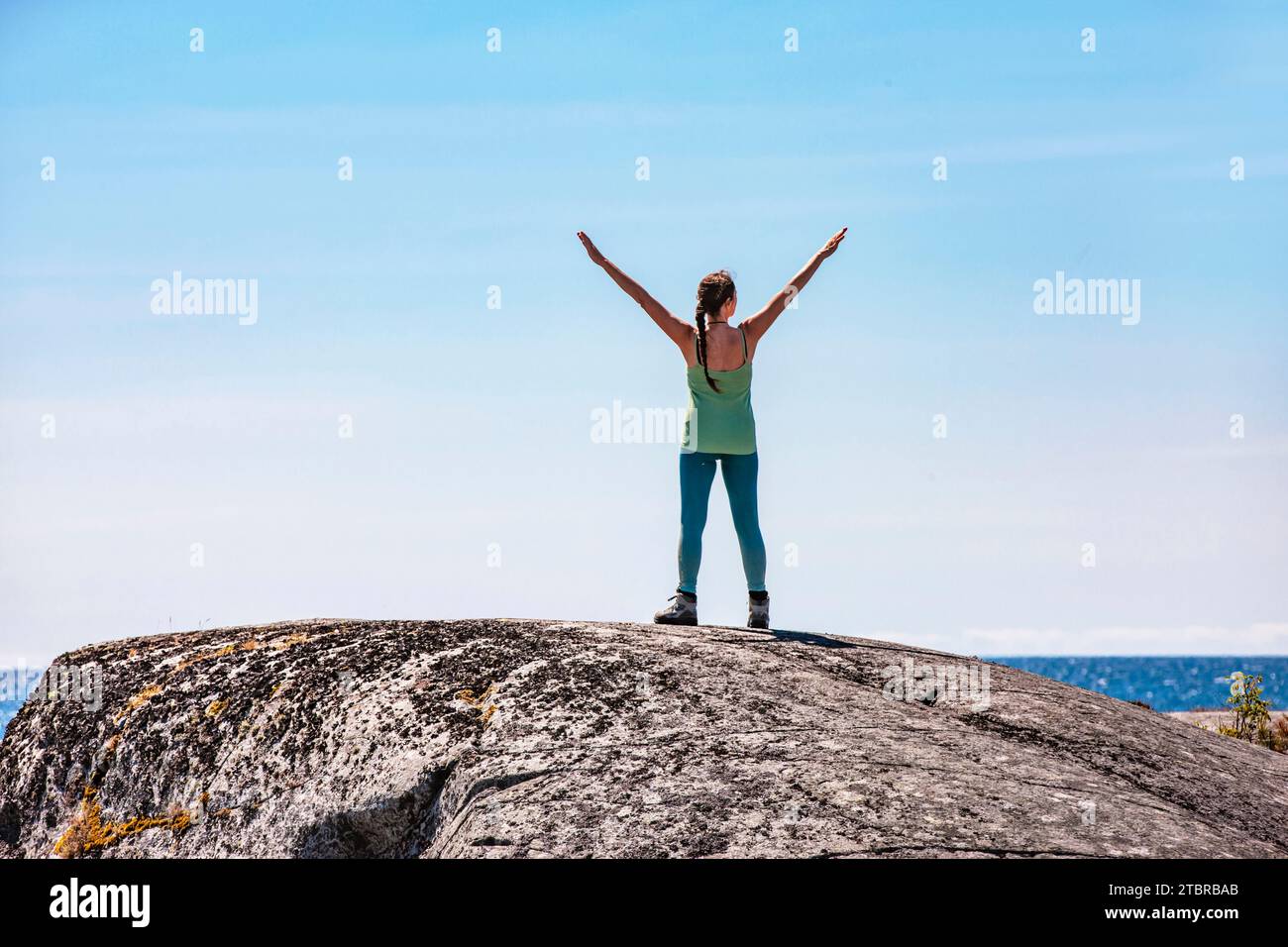Woman with outstretched arms on rocky peak by the sea hi-res stock ...