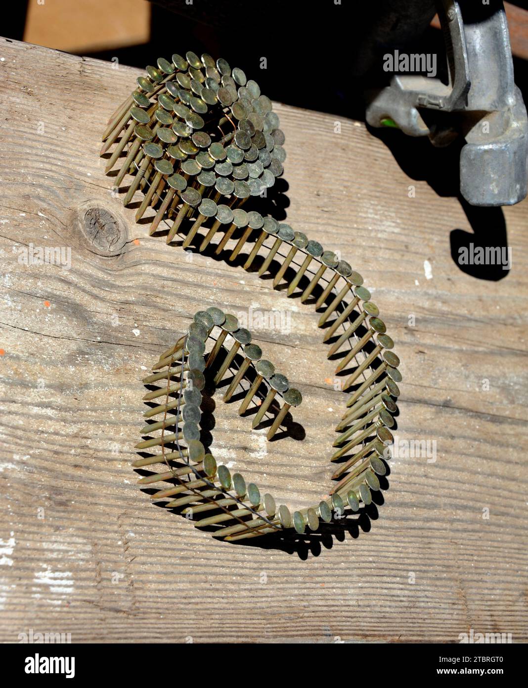 Roll of curling gun nails form the letter S. Nail roll sits on a rustic ...