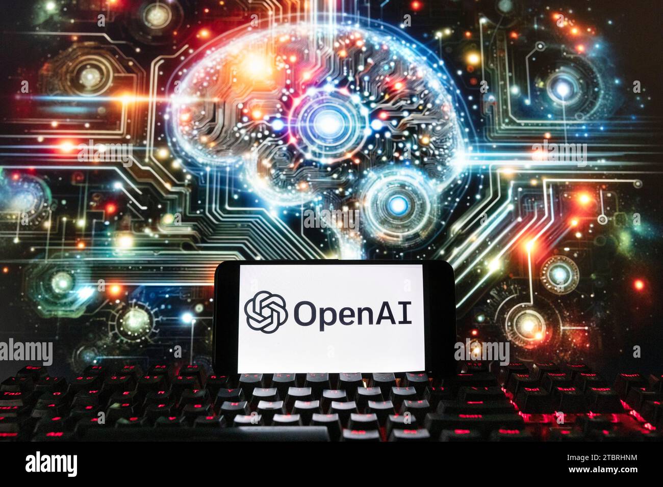 The OpenAI logo is seen displayed on a cell phone with an image on a computer screen generated ...