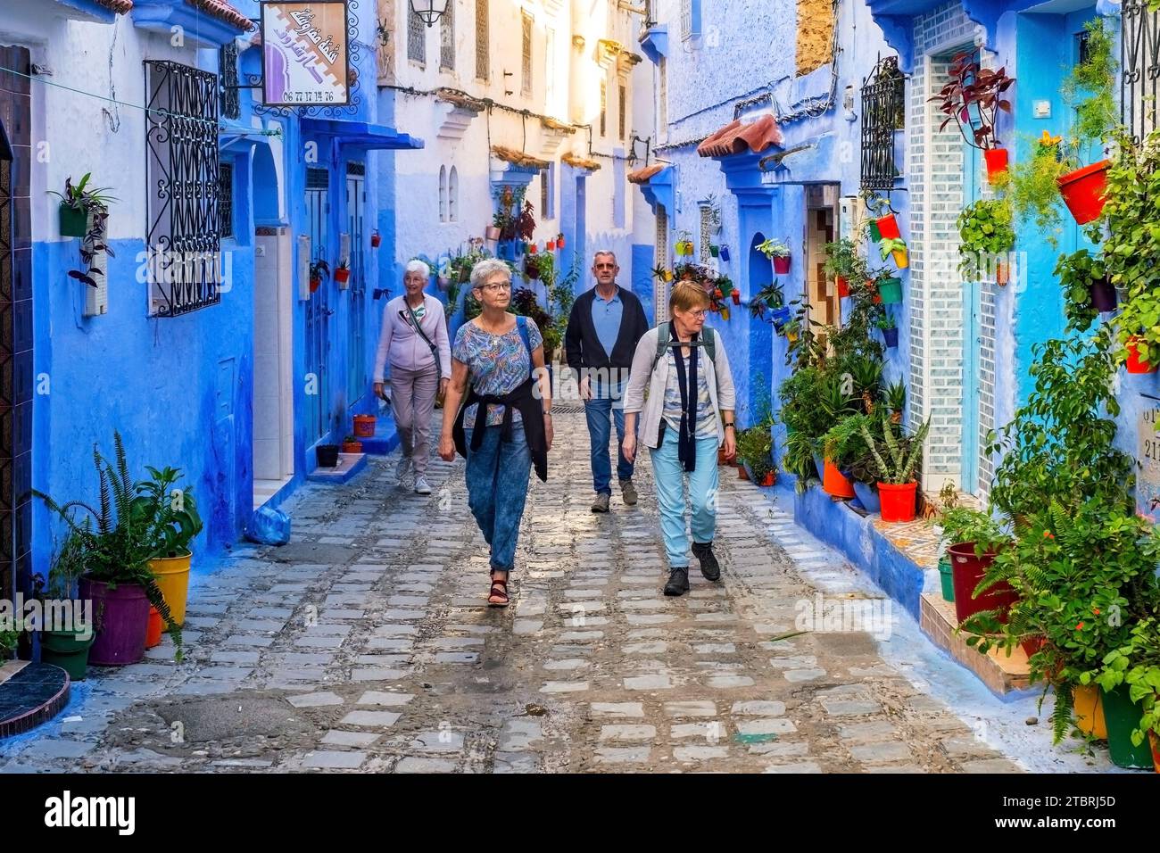 Western tourists walking in alley with blue houses in the medina ...