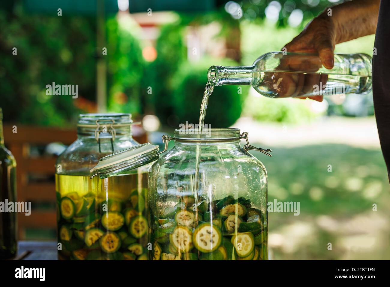 Making homemade walnut liqueur. Senior man pouring alcohol into jar ...