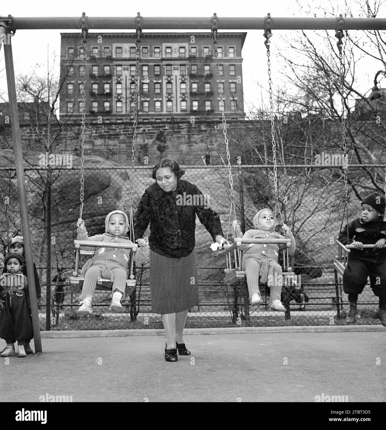 Woman pushing young children on swings at urban playground, New York ...