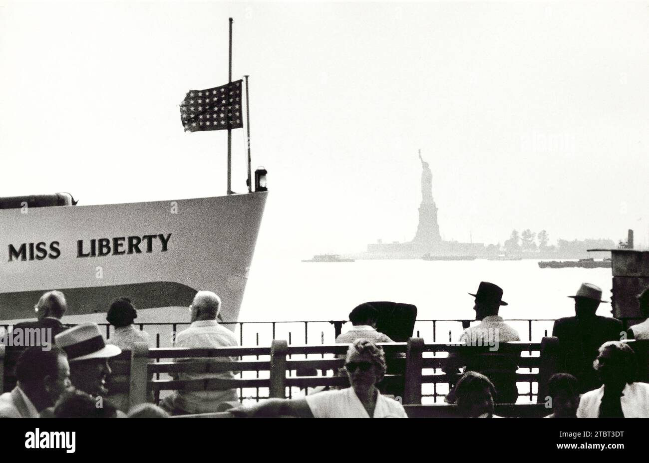 Group of people sitting on benches facing Statue of Liberty with boat ...