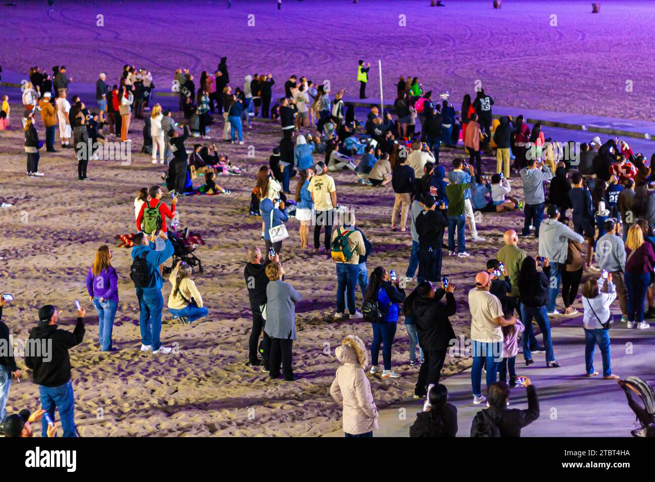A crowd of people standing on the beach at night looking up at the sky ...