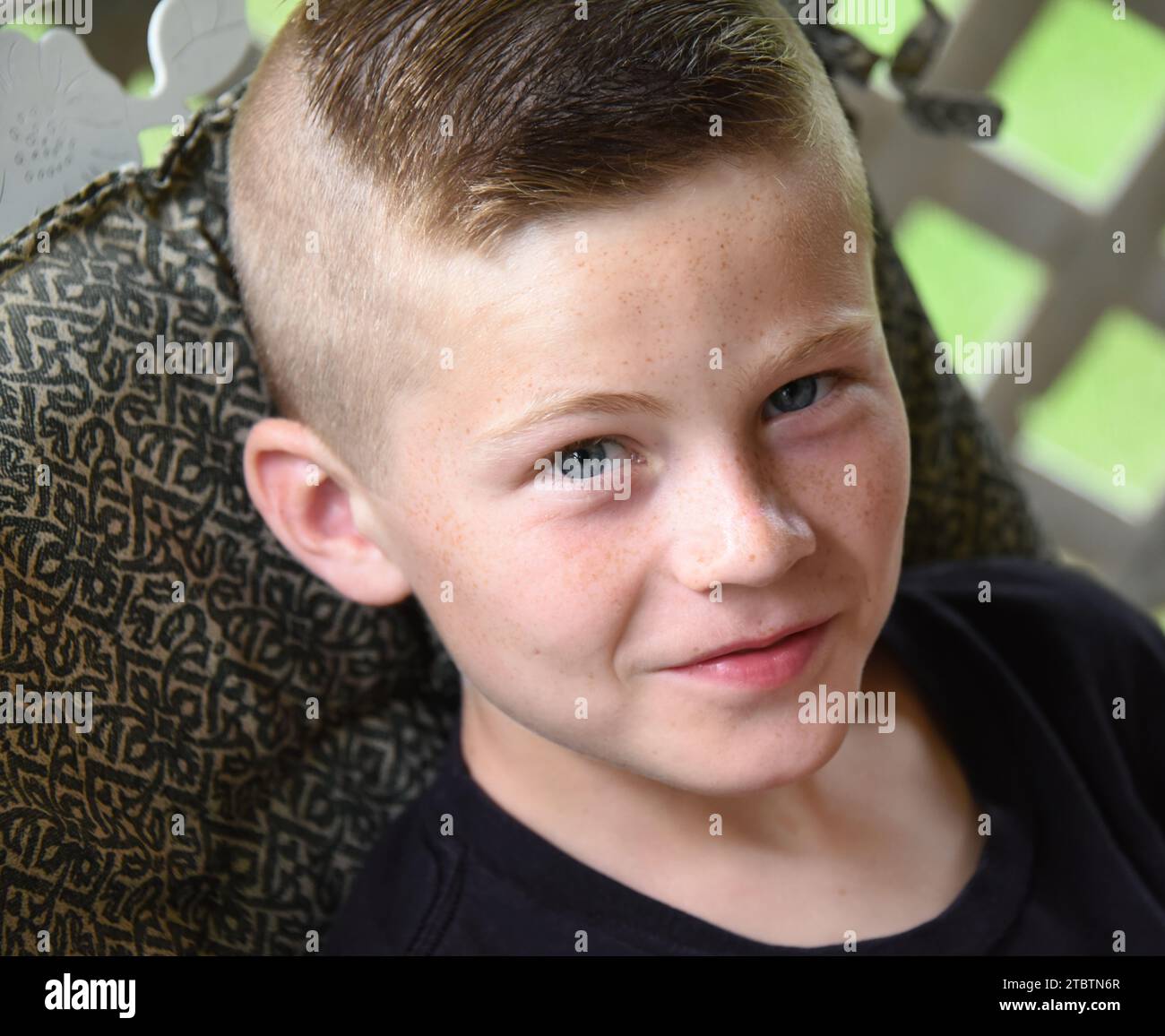 Young boy sits in a chair on patio. Image is closeup and boy looks ...