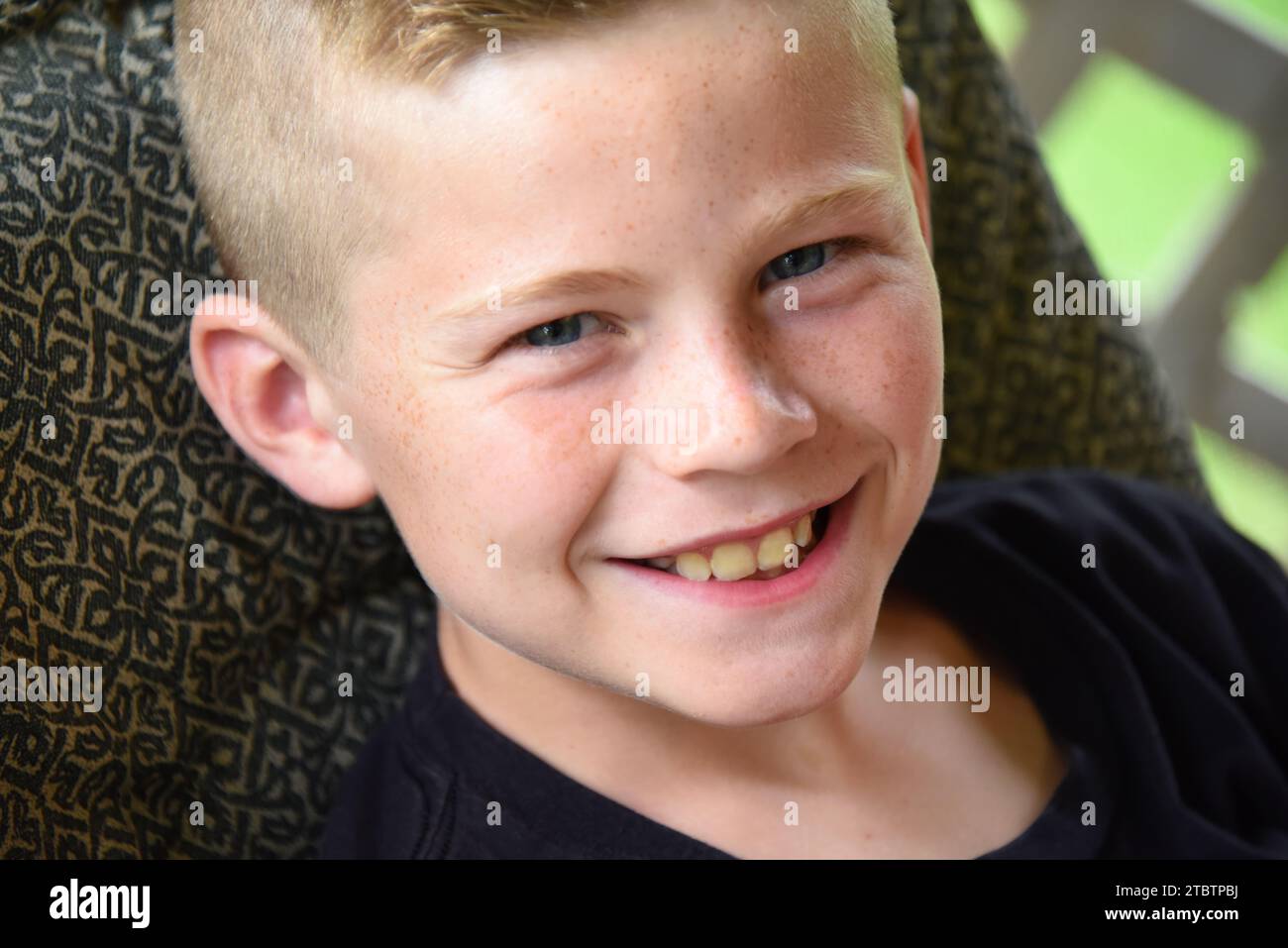 Closeup shows face of young boy grinning at the camera. He has a short ...