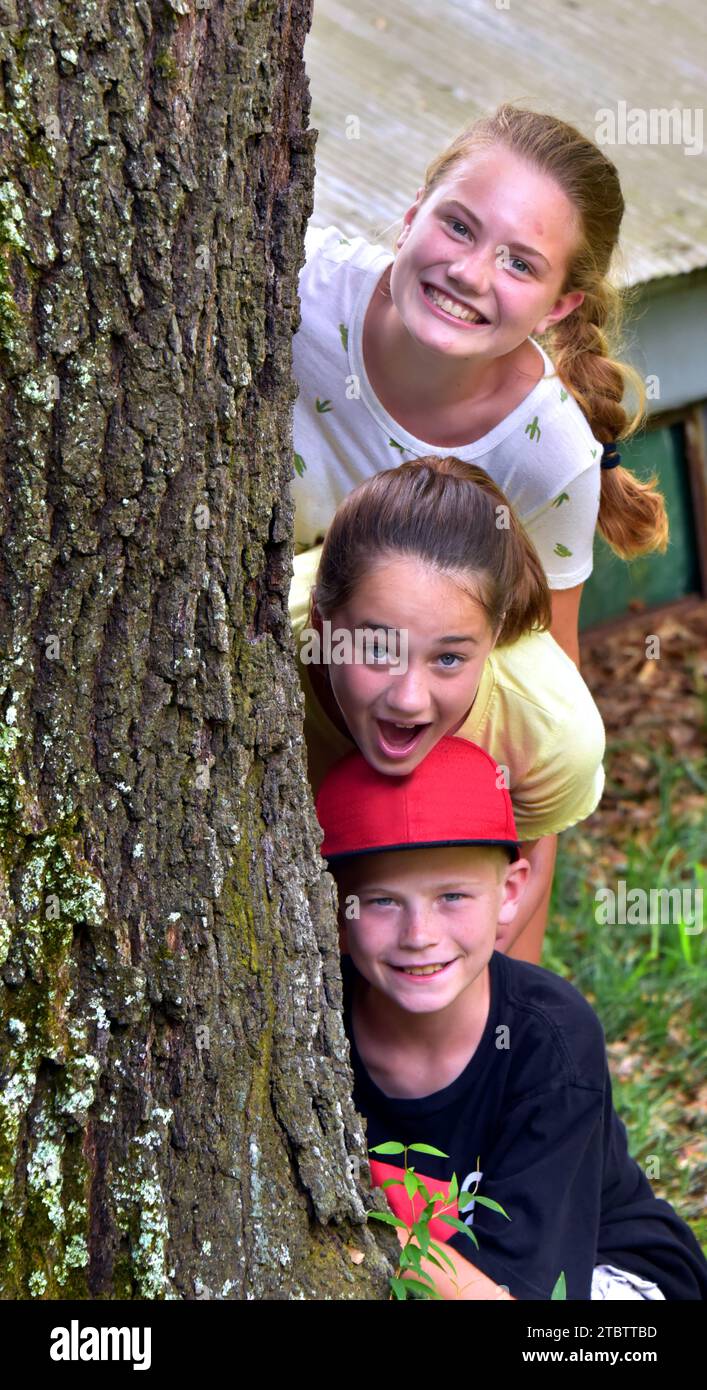 Three siblings appear behind tree as a surprise. Middle one has her ...