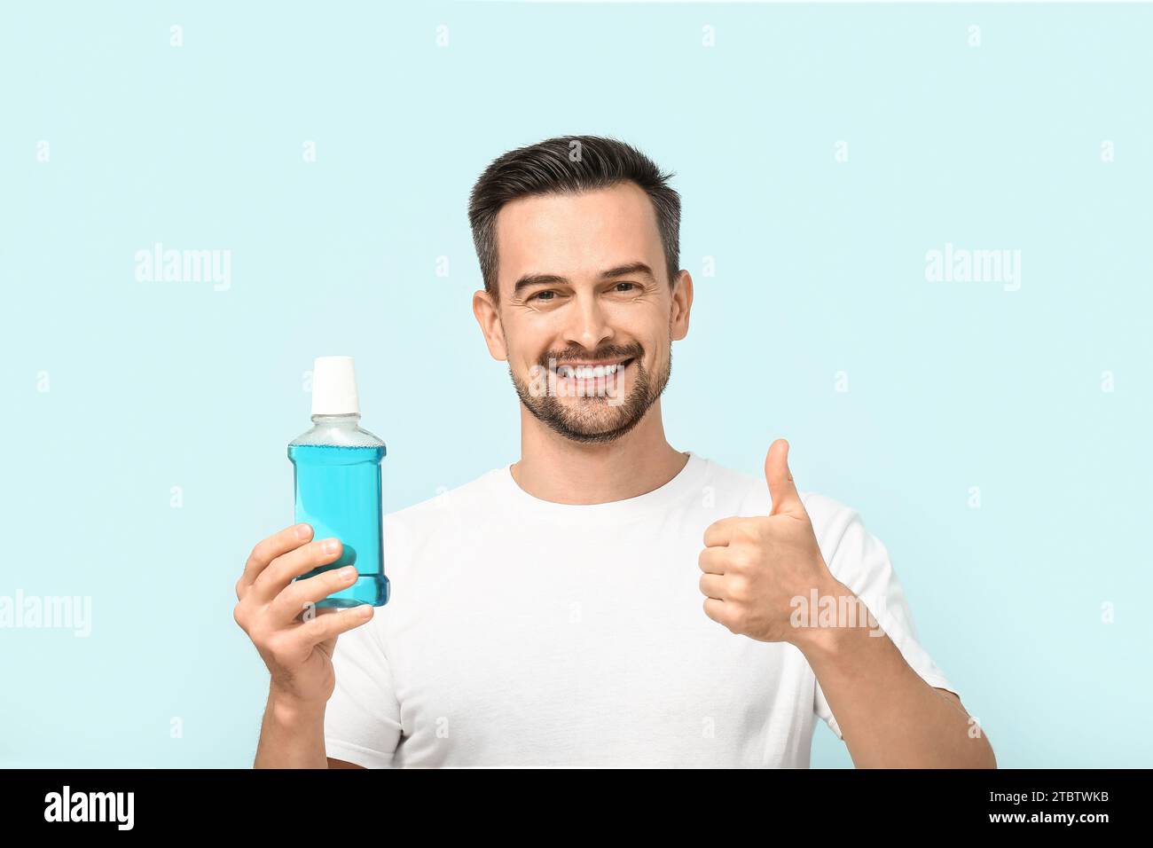 Handsome man with mouth rinse showing thumb-up on blue background Stock ...
