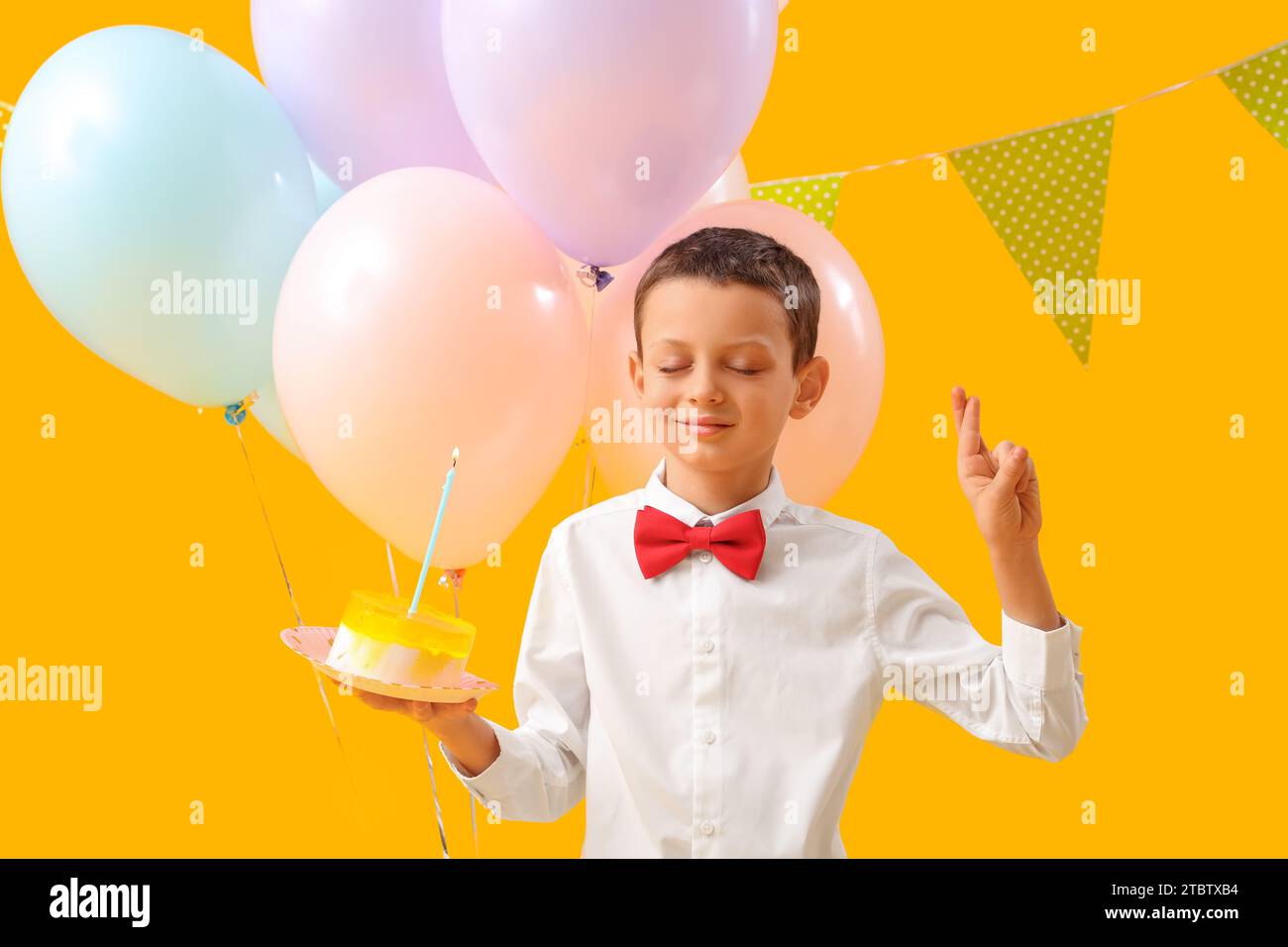 Cute little boy with cake and balloons making Birthday wish on yellow ...