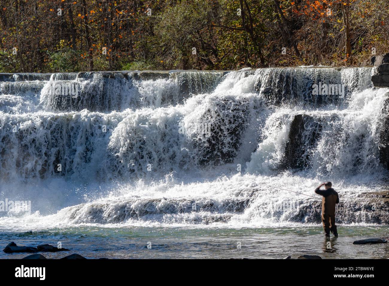 Large gushing river water fall with a fly fisherman at the bottom ...