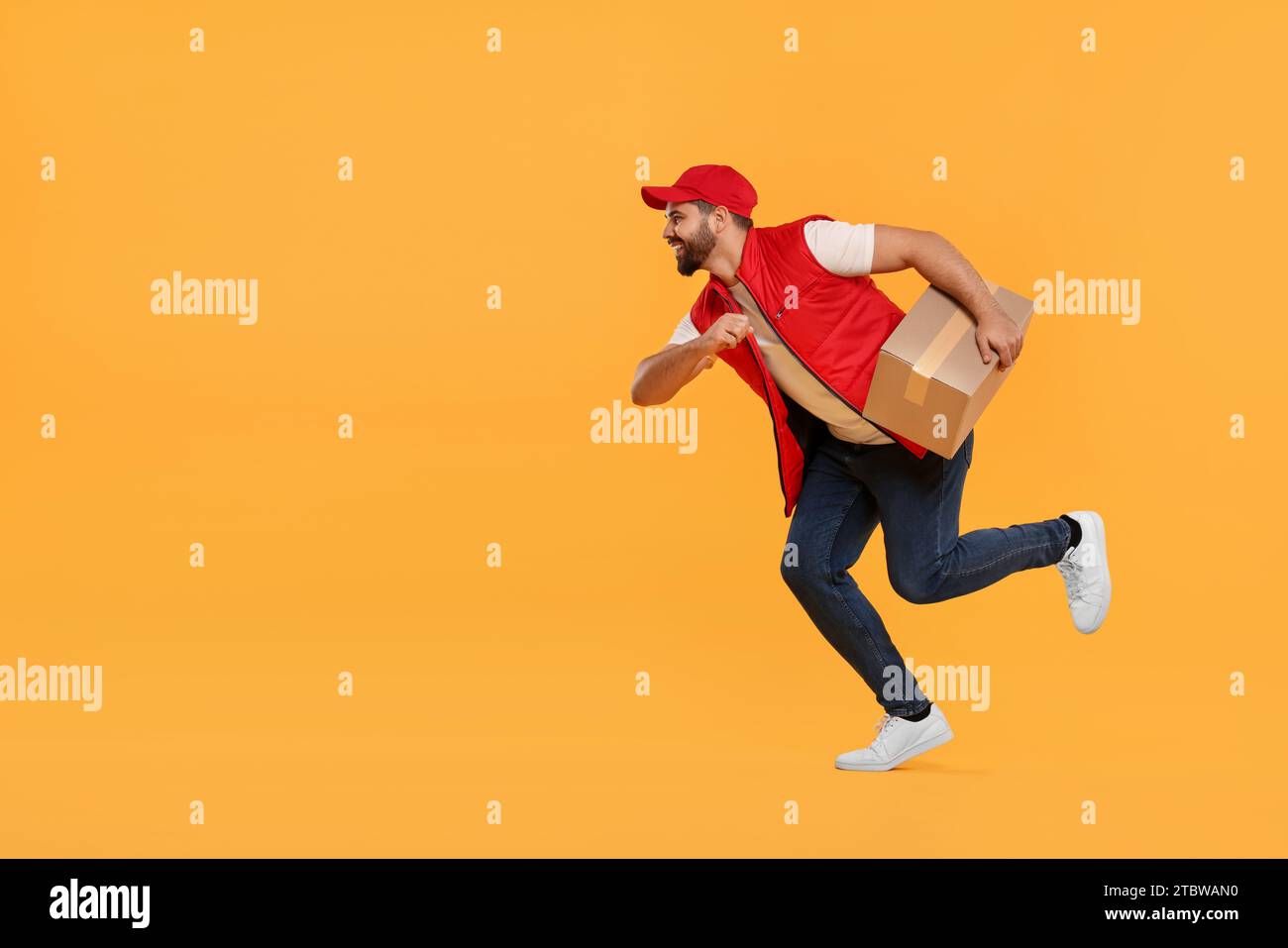 Smiling courier running to deliver parcel on orange background, space ...