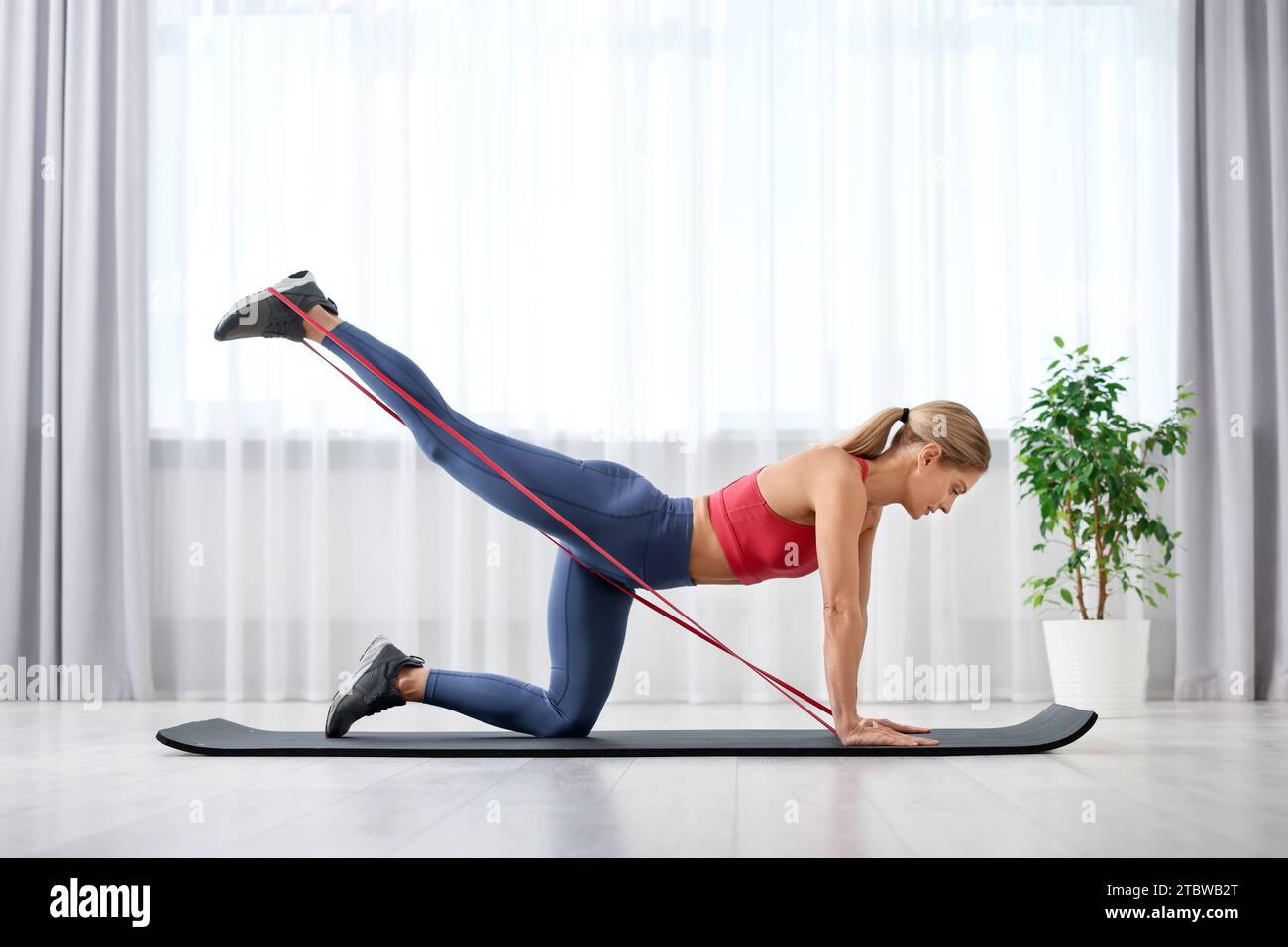 Athletic woman doing exercise with fitness elastic band on mat at home ...