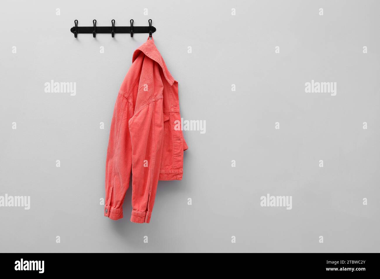 Coral jacket hanging on coat rack on light grey wall, space for text ...
