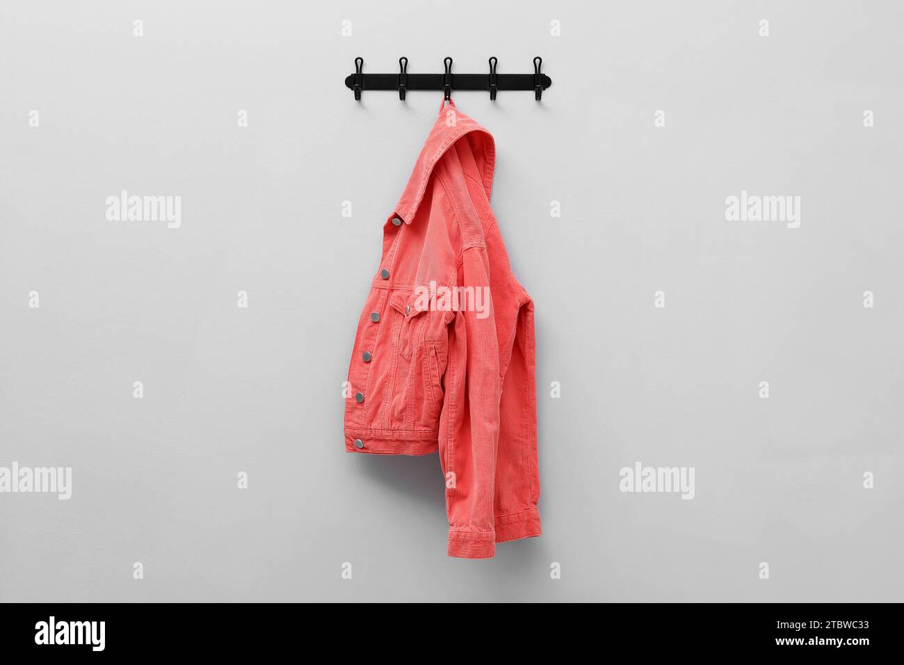 Coral jacket hanging on coat rack on light grey wall Stock Photo - Alamy