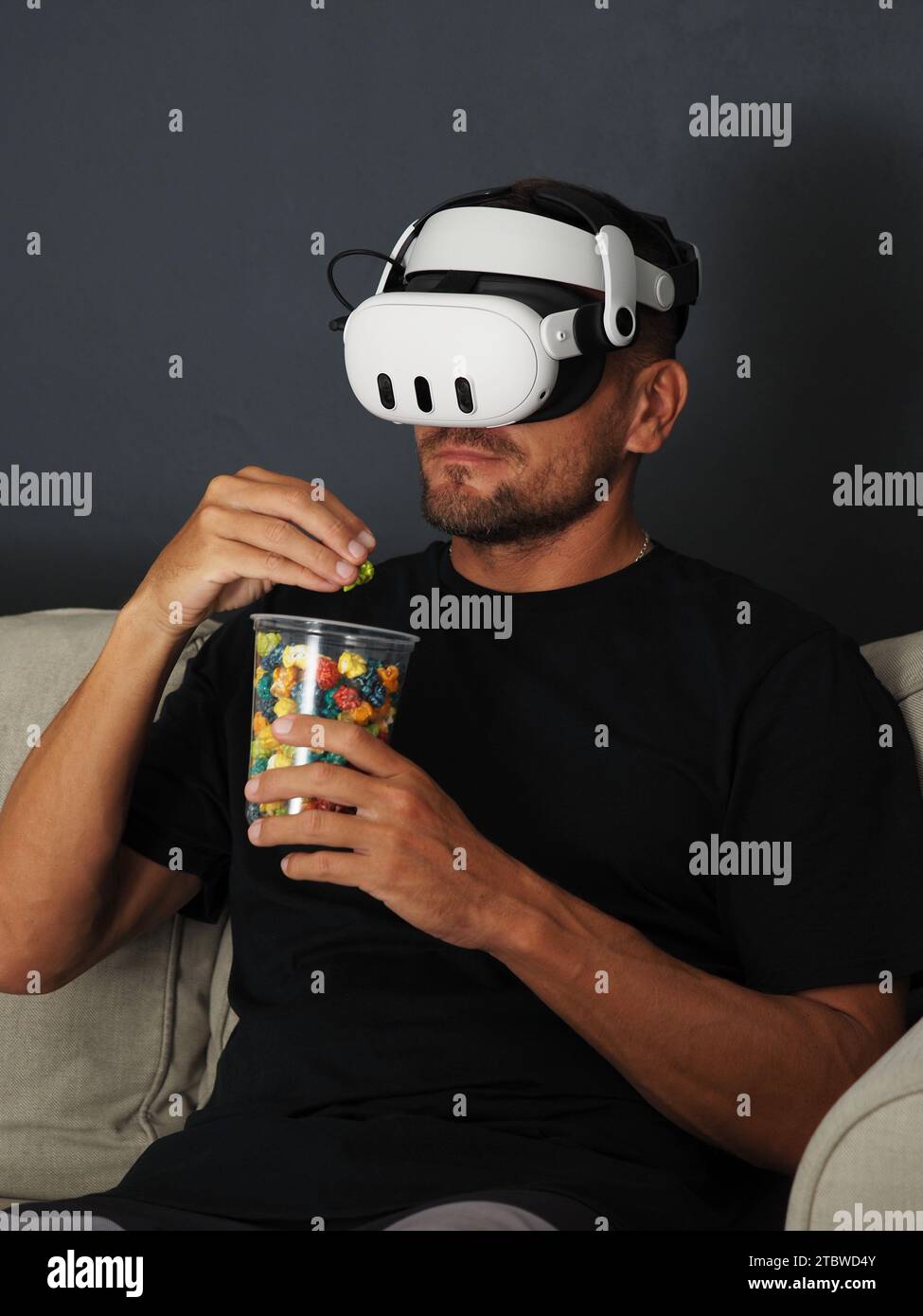 Man wearing VR goggles sitting on sofa eating popcorn watching 3d movie ...