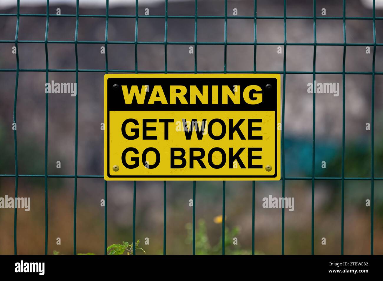 Warning sign on a fence stating in "Warning - Get woke, go broke Stock ...