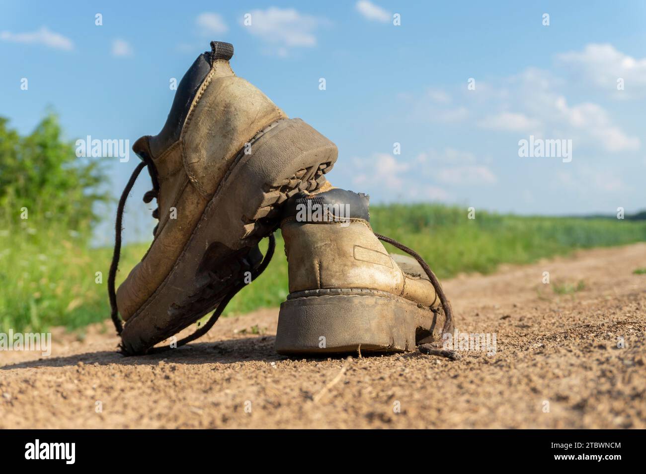 Pair of old worn leather hiking boots an a gravel path or road balanced ...