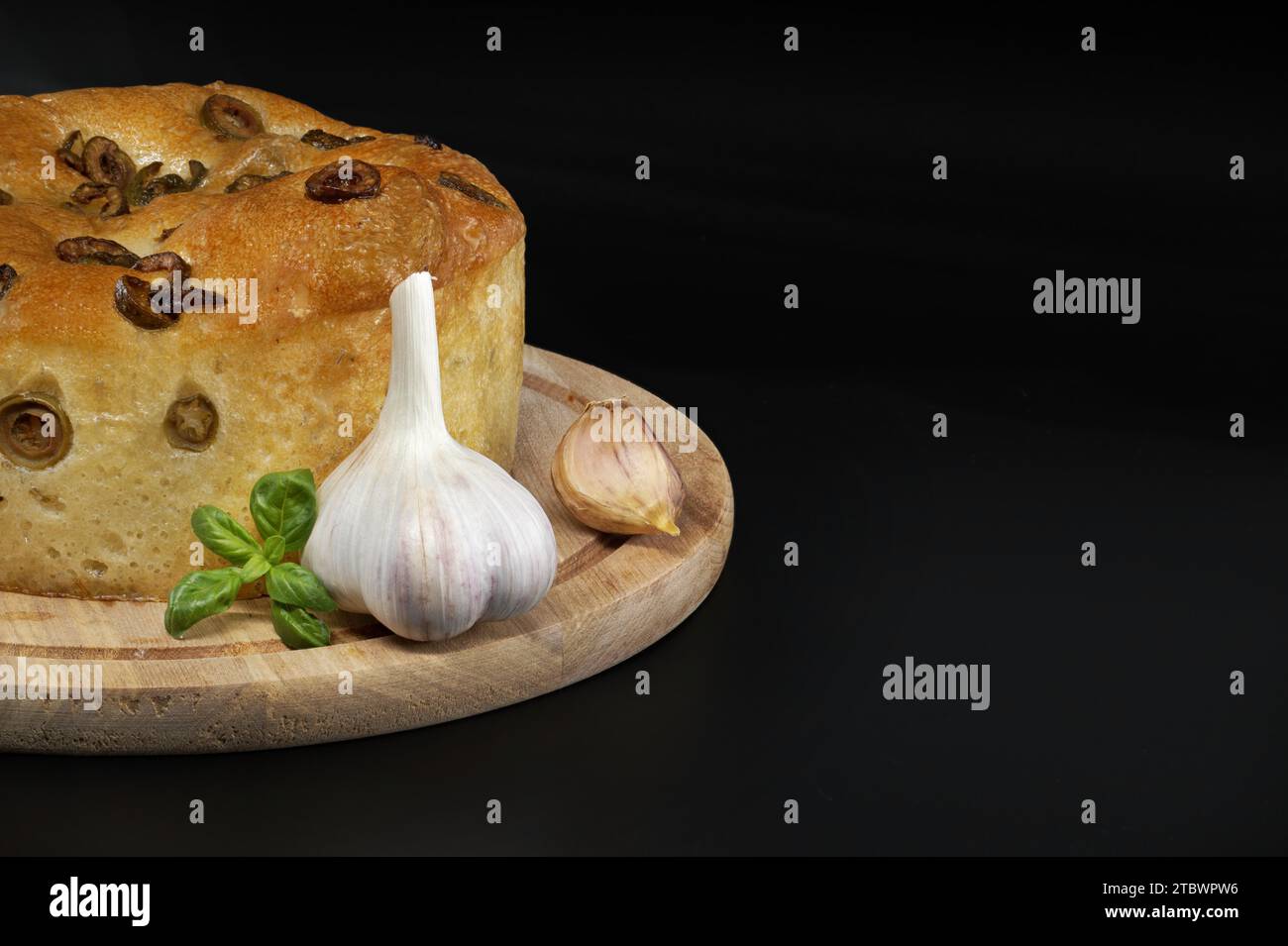 Round focaccia bread with olives, garlic and basil sprig over black ...