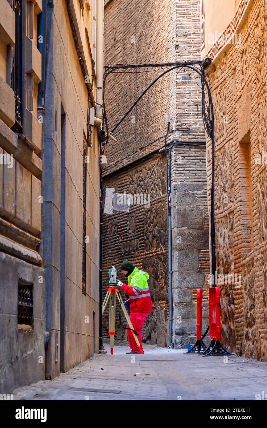 A surveyor man using a theodolite instrument or tool in a narrow street ...