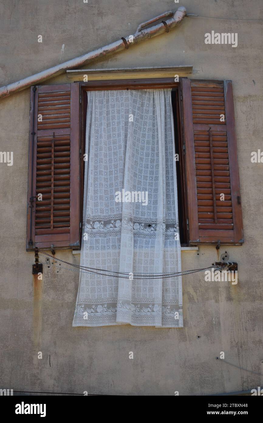 White embroidered curtain hanging through window with open brown wooden ...