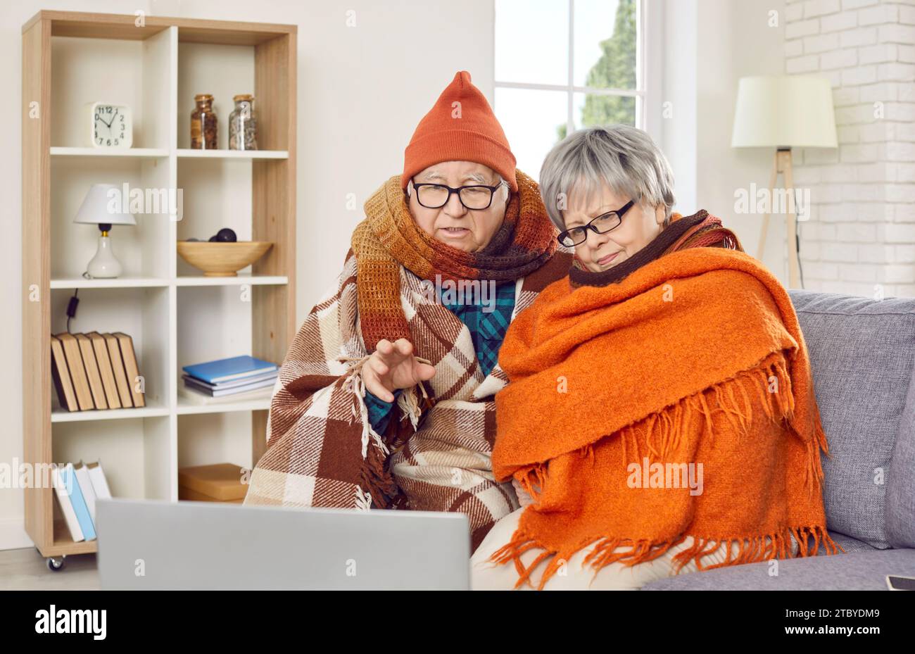 Sick frozen senior couple sitting on sofa and having online video call ...