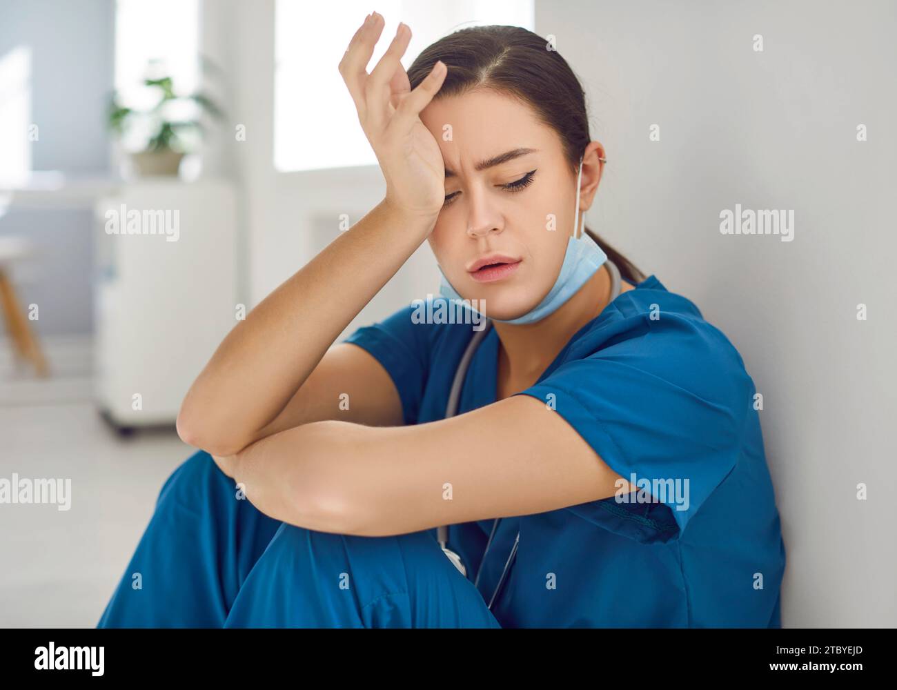 Tired depressed female nurse wearing blue face mask and uniform sitting ...
