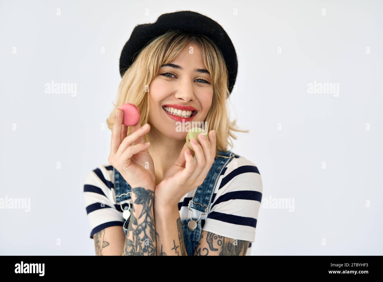 Happy pretty gen z blonde girl having fun holding macaroons isolated ...