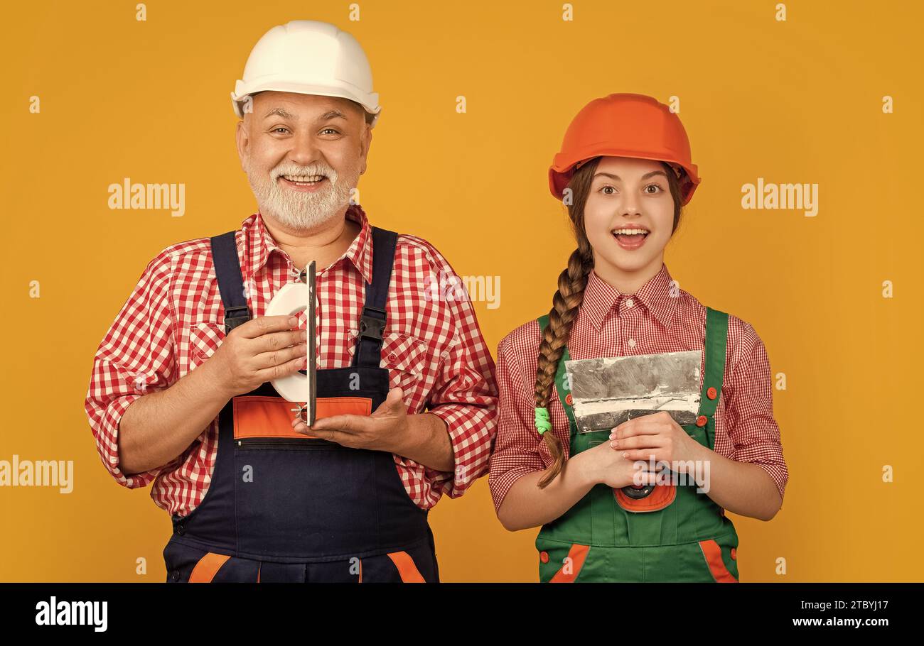 happy girl and grandfather plasterer in helmet on yellow background ...