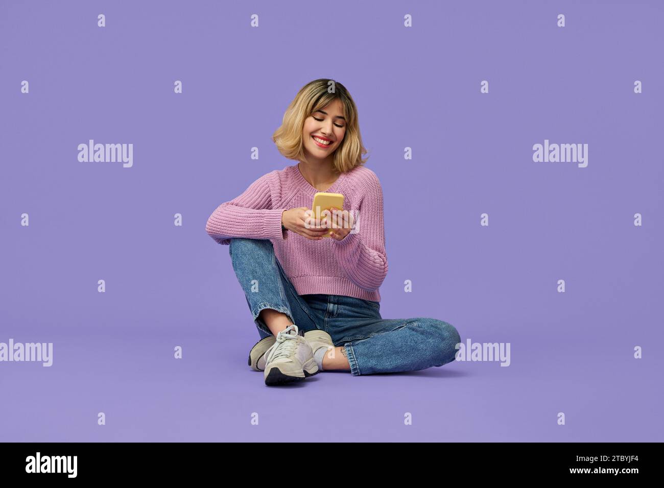 Happy pretty gen z blonde girl using mobile phone isolated on purple ...