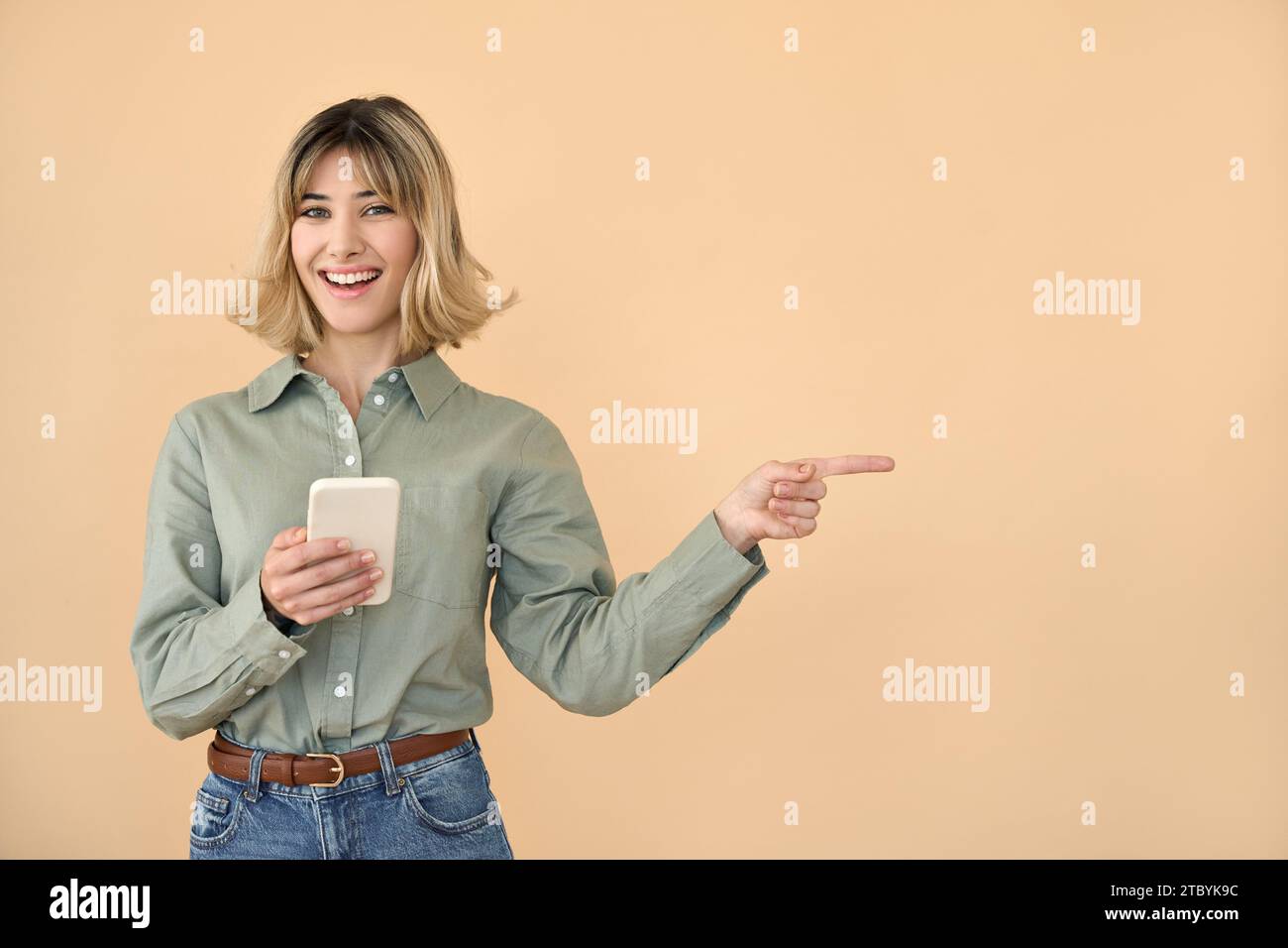 Happy gen z young woman using phone pointing aside isolated on ...