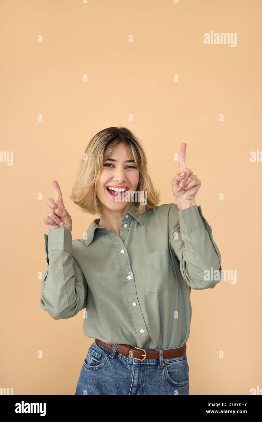 Excited gen z blonde young woman pointing up isolated on beige ...