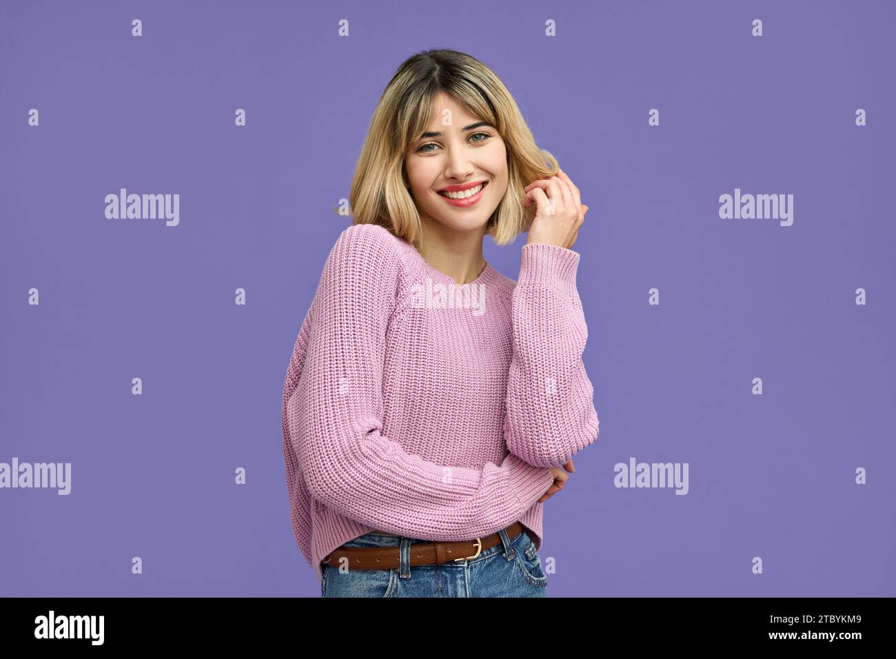 Happy gen z blonde girl in pink sweater standing isolated on purple ...