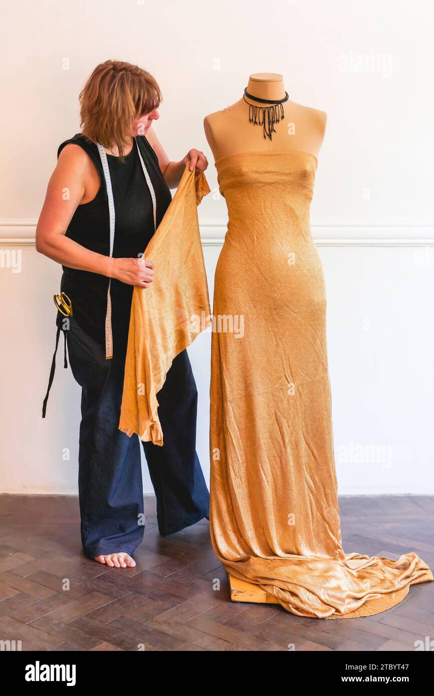 Fashion designer working on a garment and a dress hanging over a ...