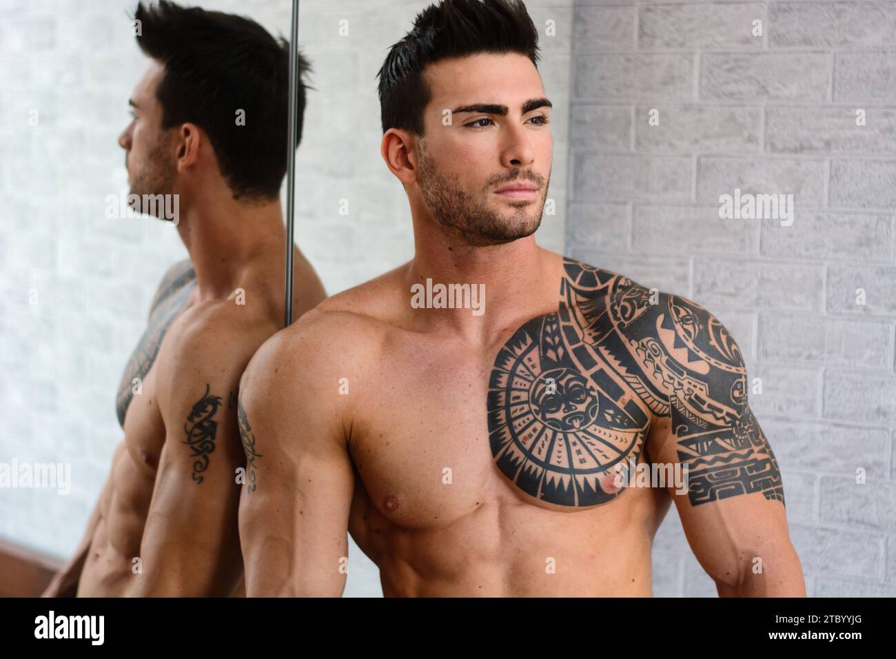 A handsome muscular man with tattoos standing in front of a mirror ...