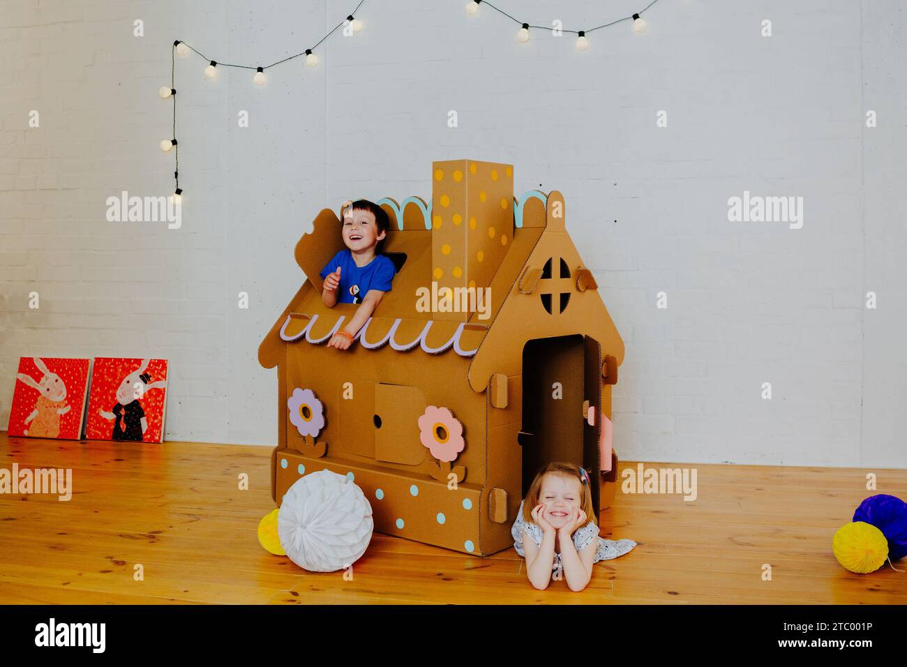 Joyful siblings running after each other and around cardboard house ...