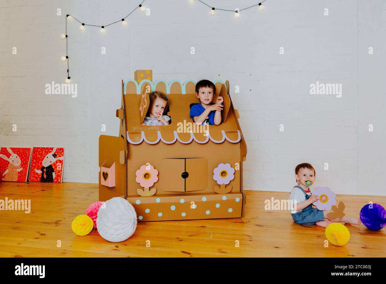 Joyful siblings running after each other and around cardboard house ...