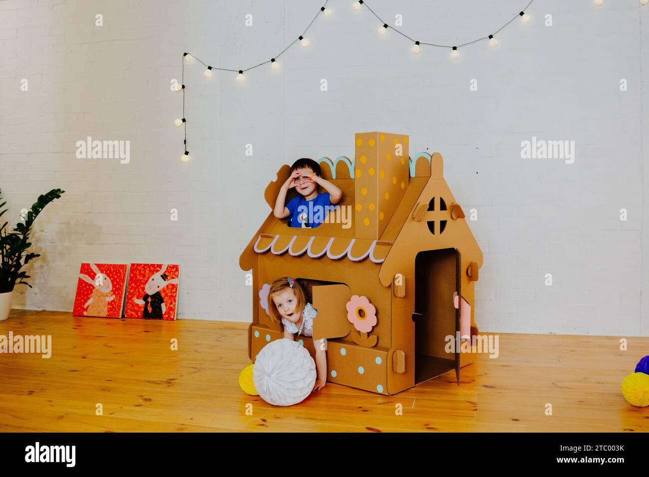 Joyful siblings running after each other and around cardboard house ...