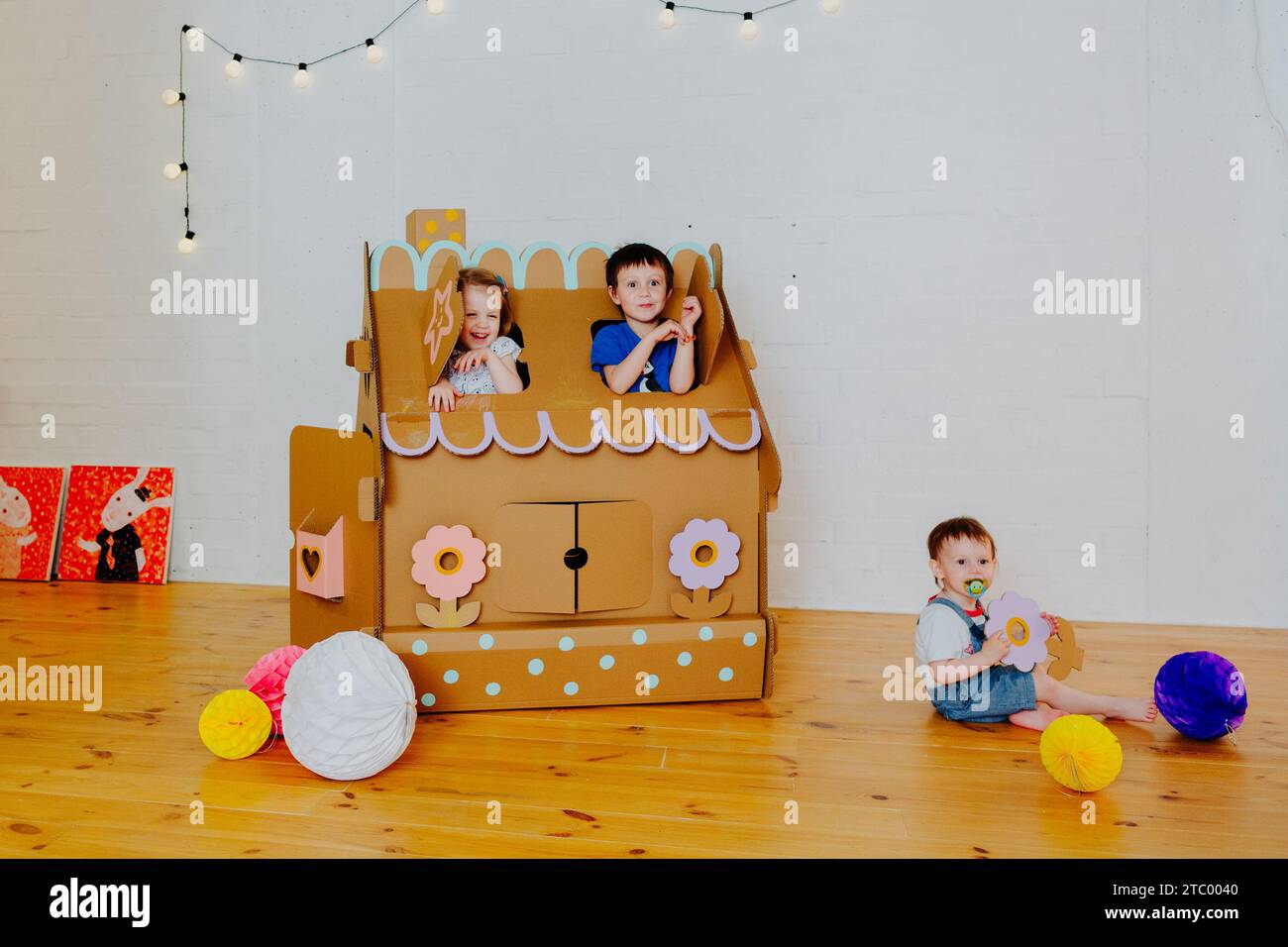 Joyful siblings running after each other and around cardboard house ...