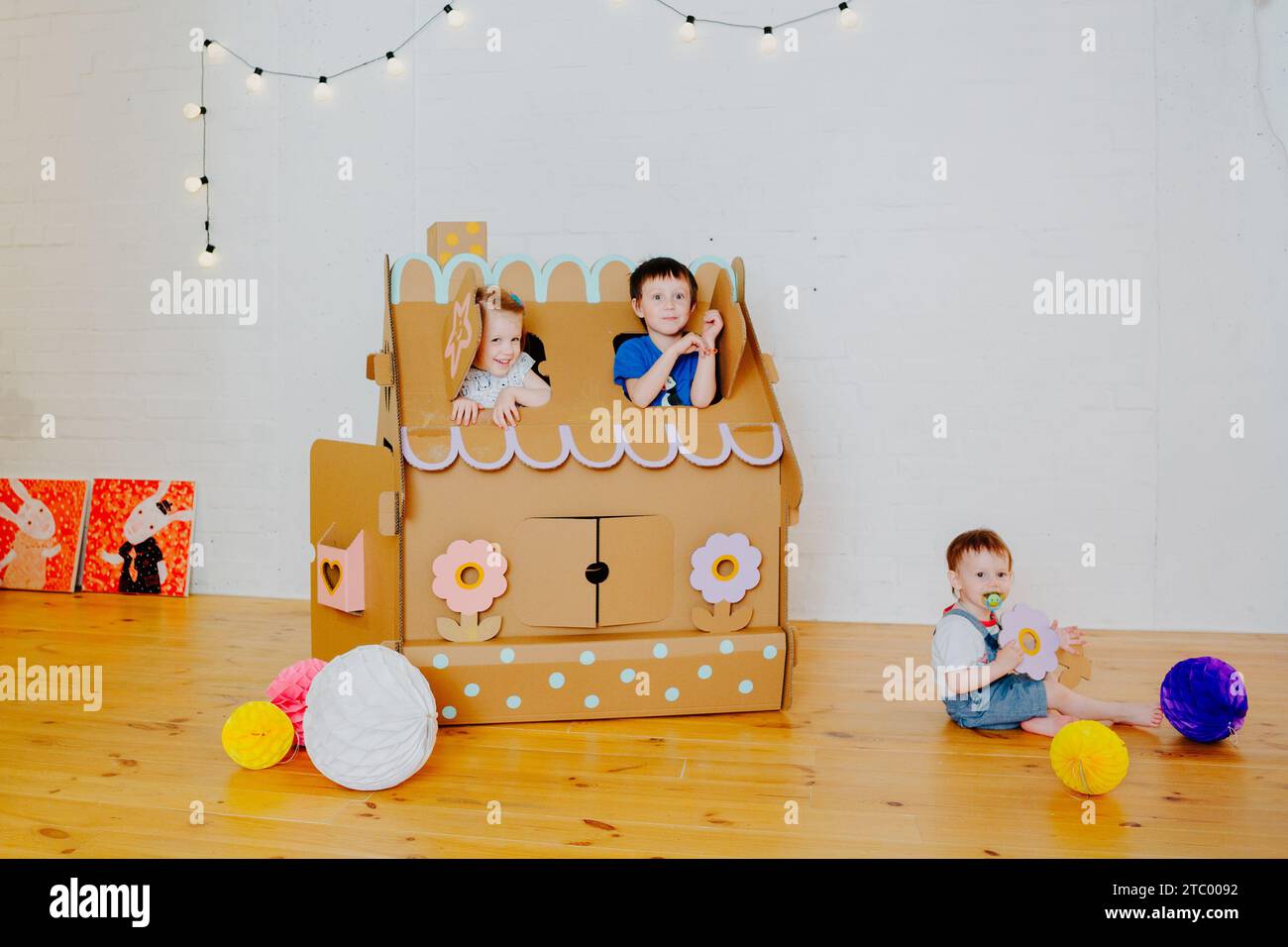 Joyful siblings running after each other and around cardboard house ...