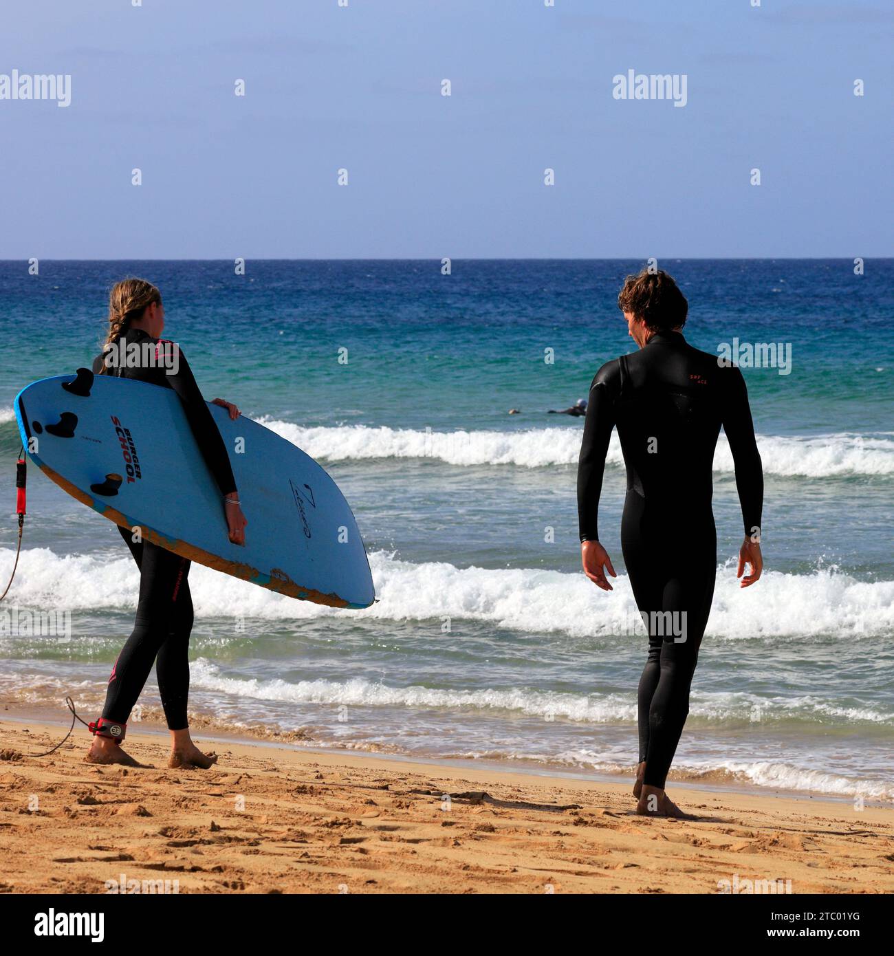Man and woman in wet suits with surfboard walking towards the sea, El ...